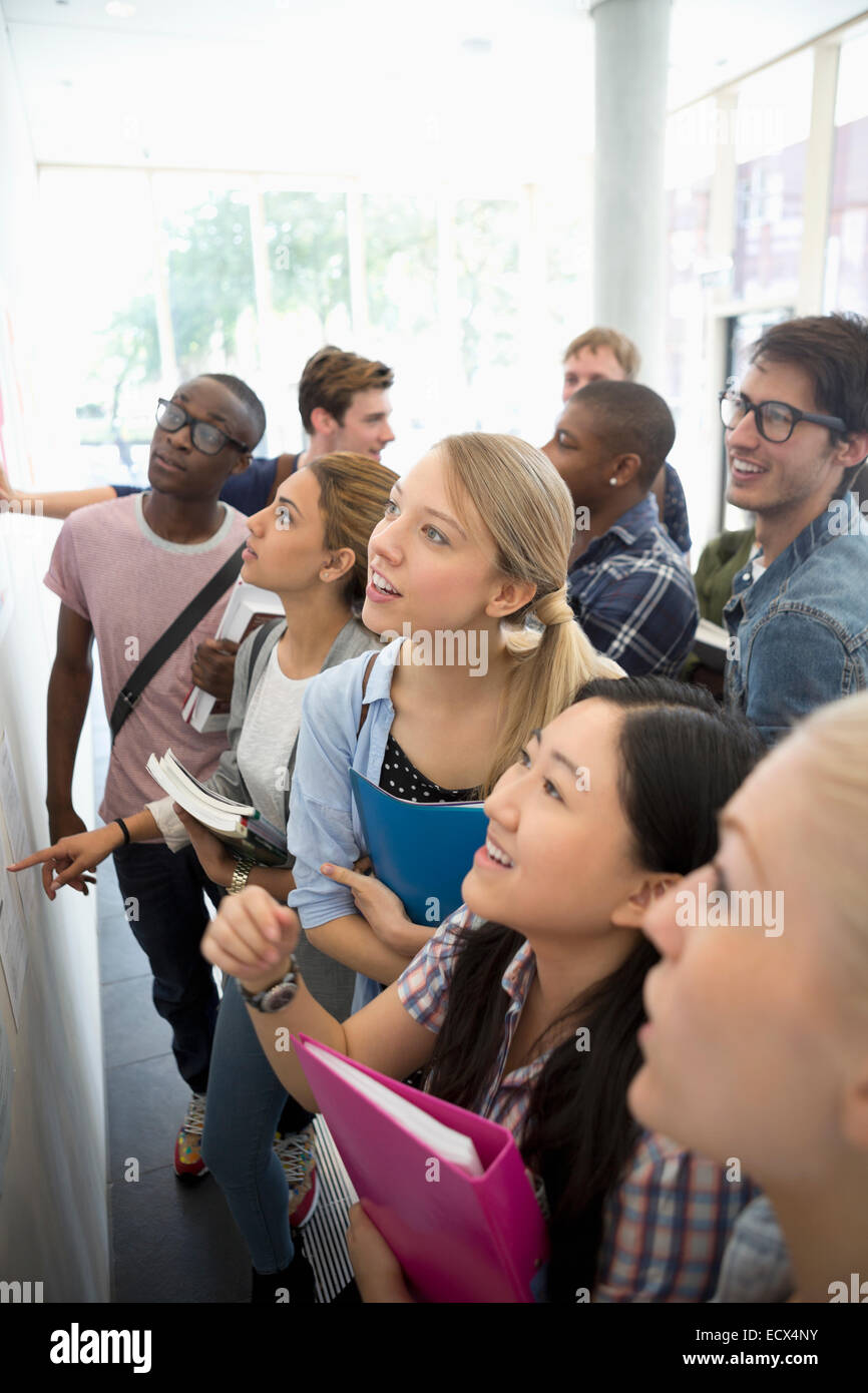 Elevated view of group of students looking at notice board during break ...