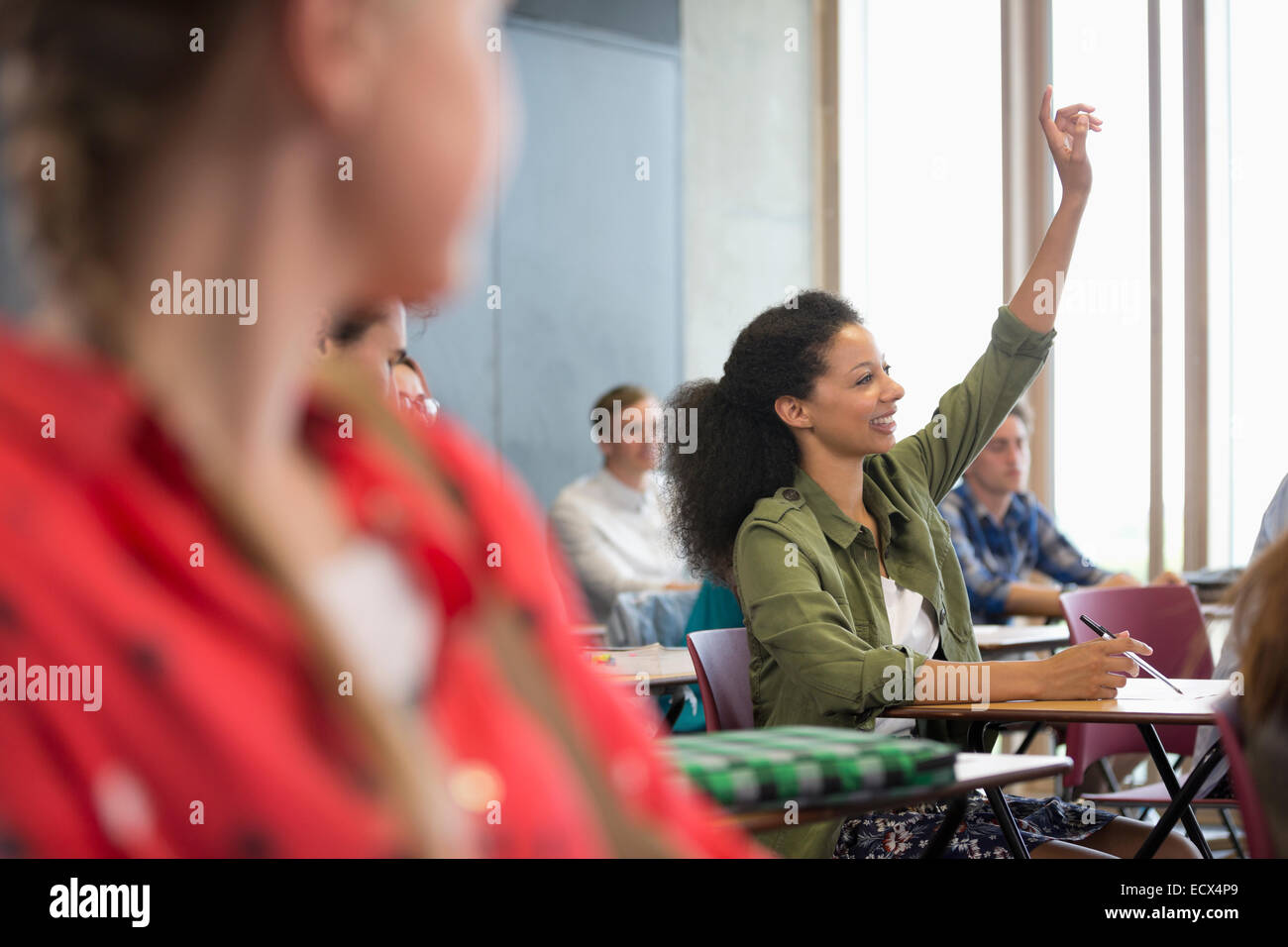 Female student raising hand during lecture with other students in ...