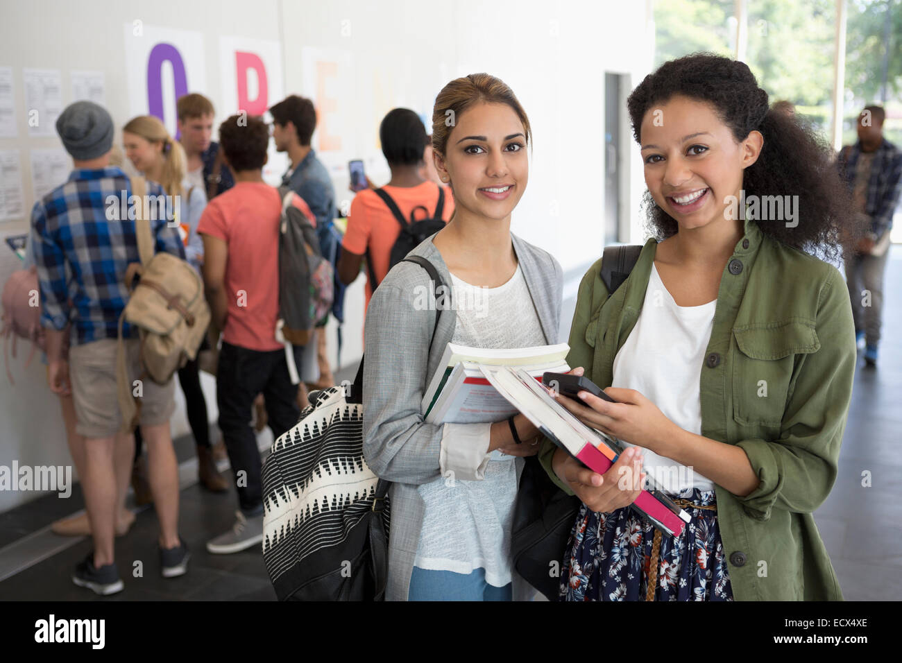 Portrait of two smiling female students holding books, other students ...