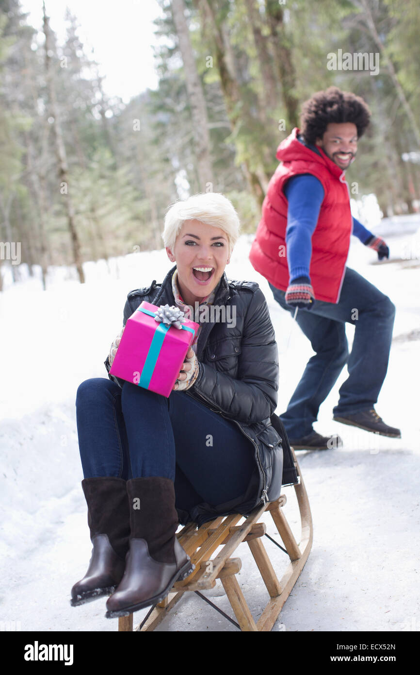 Man pulling woman with gift on sled in snow Stock Photo - Alamy