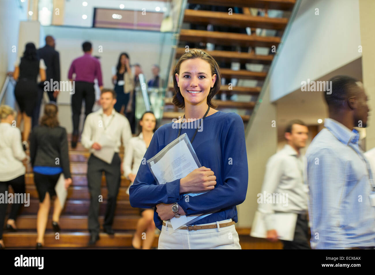 Portrait of smiling young woman standing in lobby of conference center ...