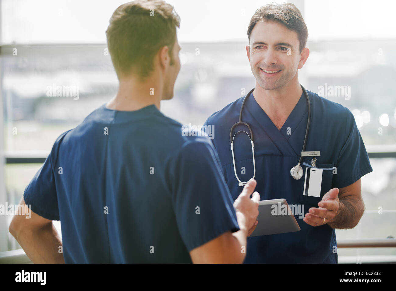 Two doctors talking, one holding tablet pc Stock Photo - Alamy