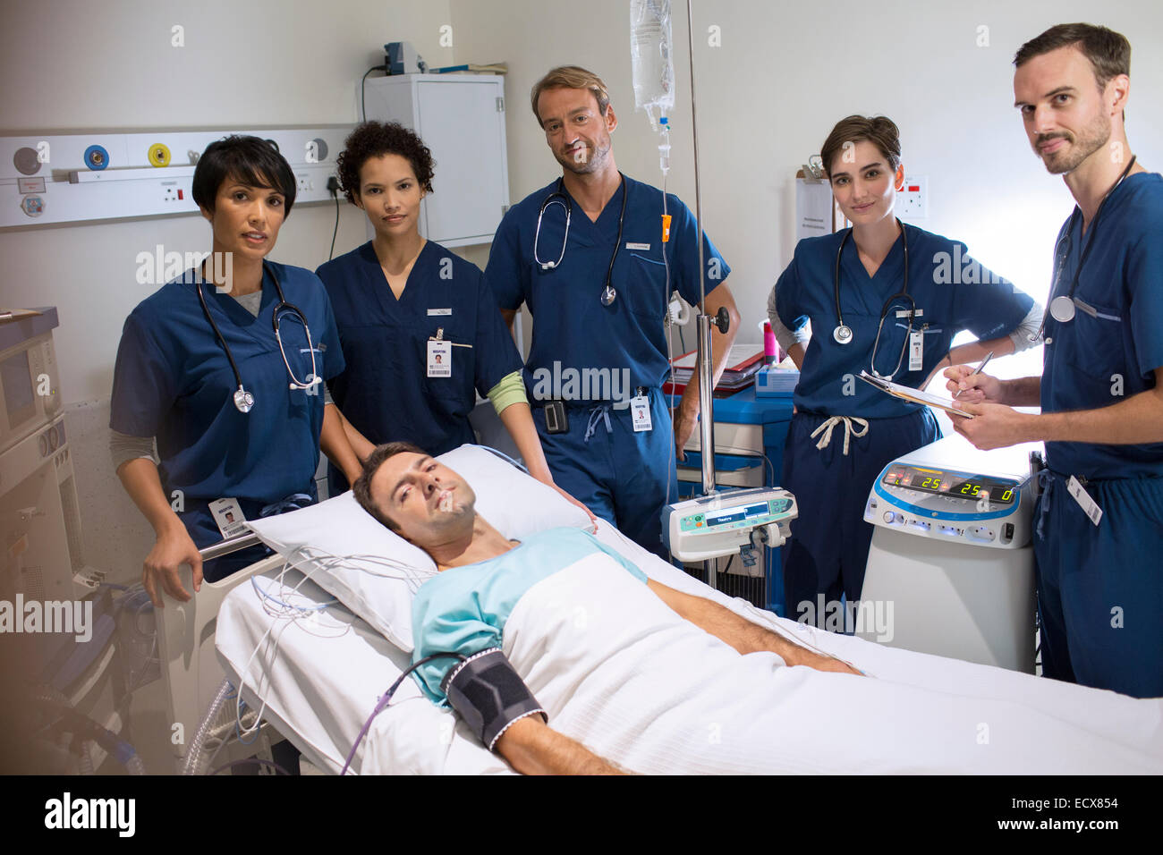 Team of doctors standing around smiling patient lying in bed in ...