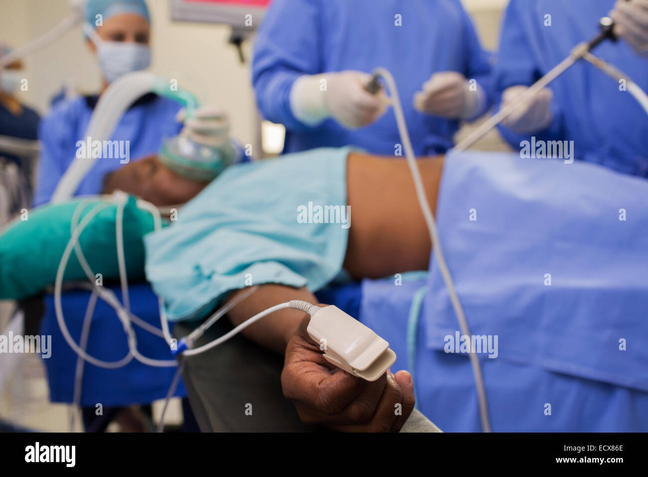 Doctors performing laparoscopic surgery, patient with pulse oxymeter on ...