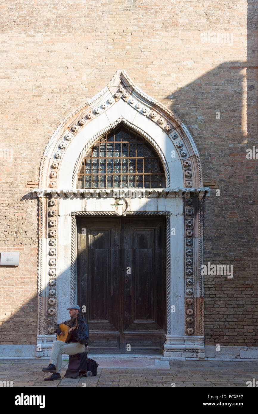 A musician plays an old instrument outside a church door in Venice ...
