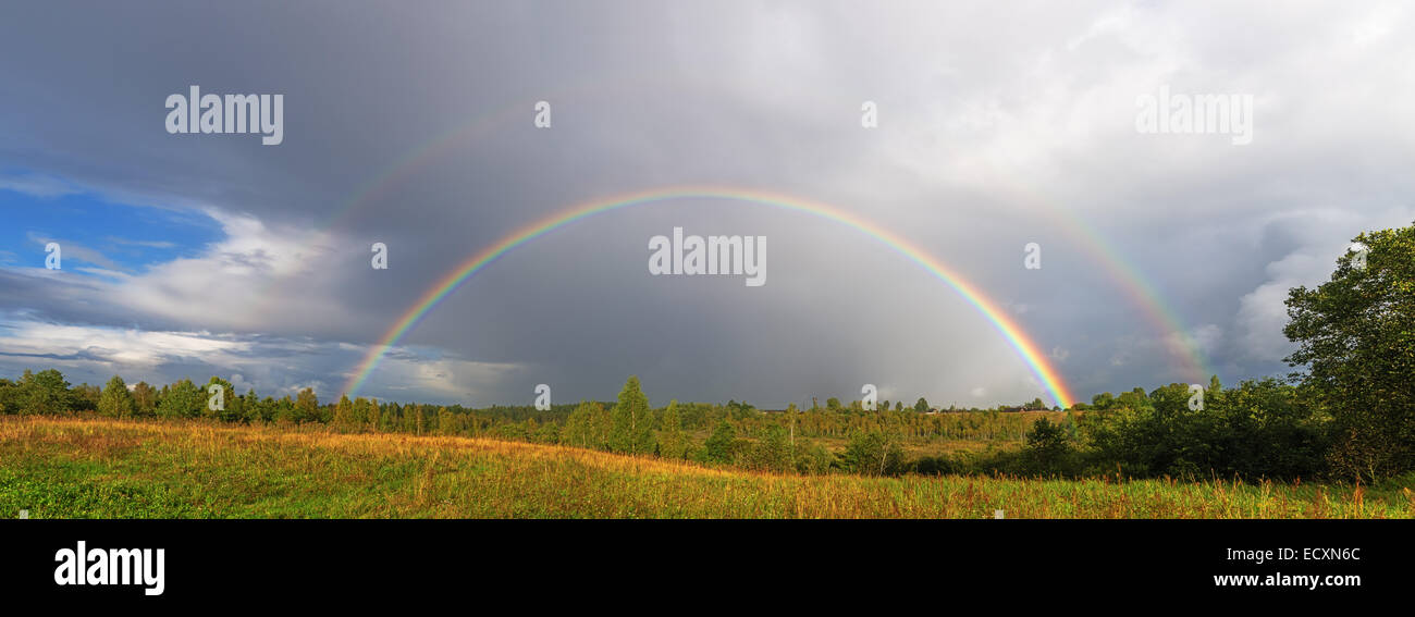 A bright double rainbow arches over a village field Stock Photo - Alamy