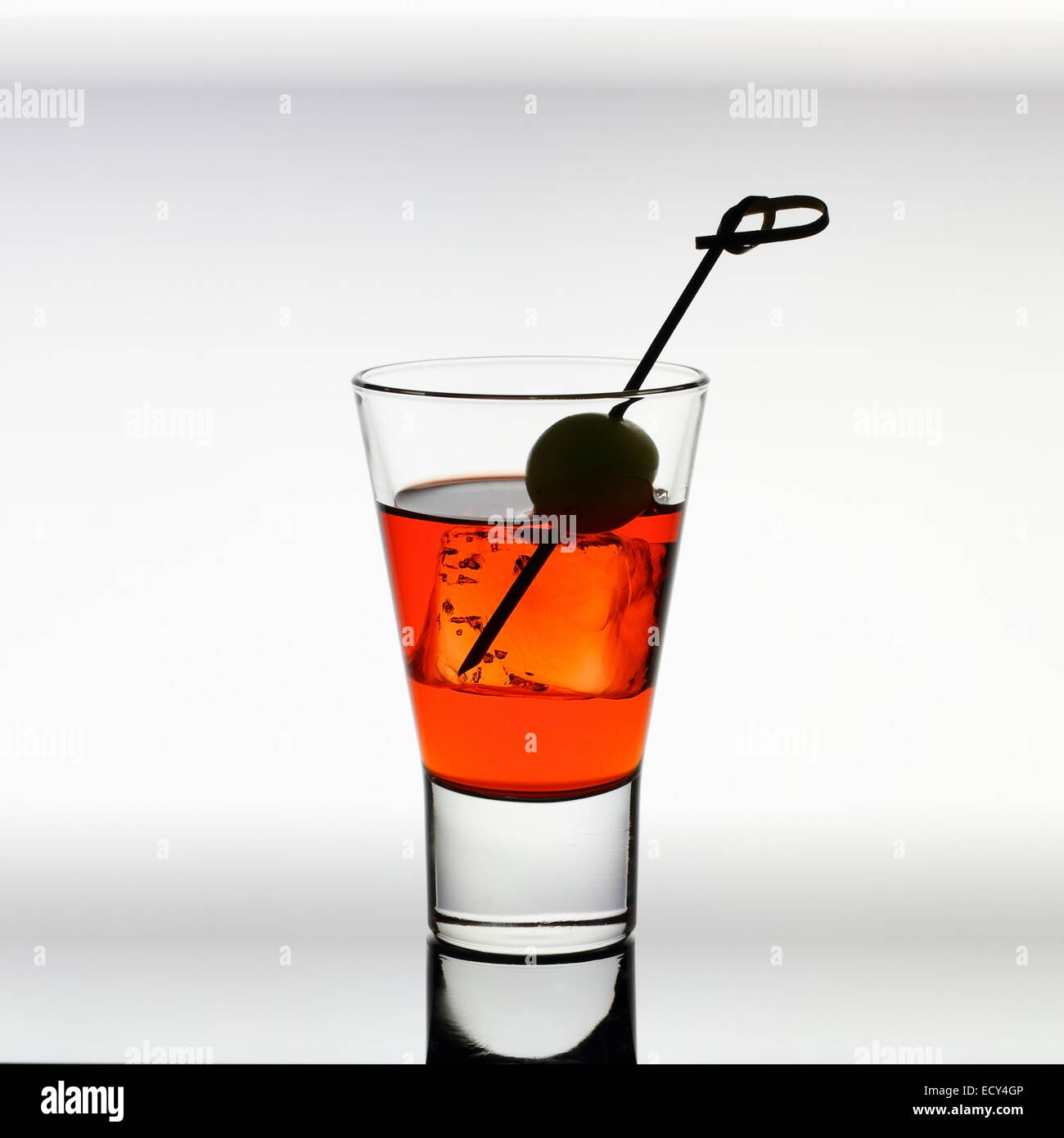 Short drink glass with red liquid, olive, ice cubes, gray background ...