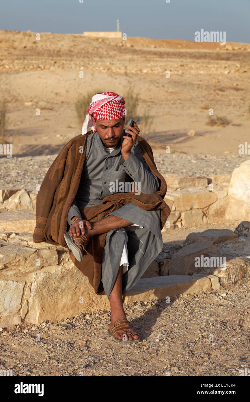 Jordanian in traditional dress on a mobile phone, desert castle Qasr ...