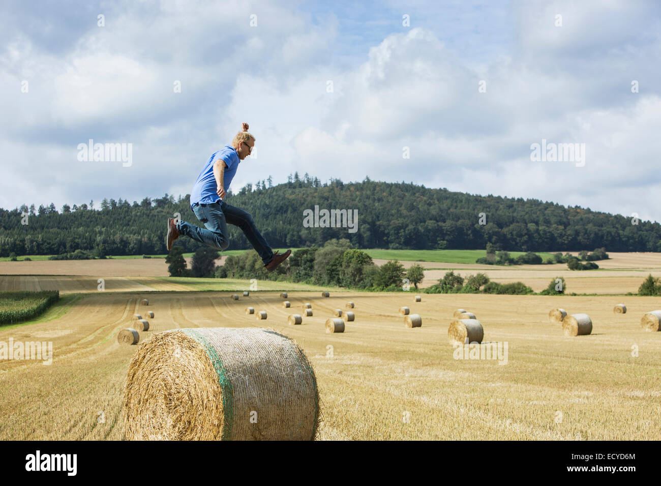 Farmer jumping over hay bale in field Stock Photo - Alamy