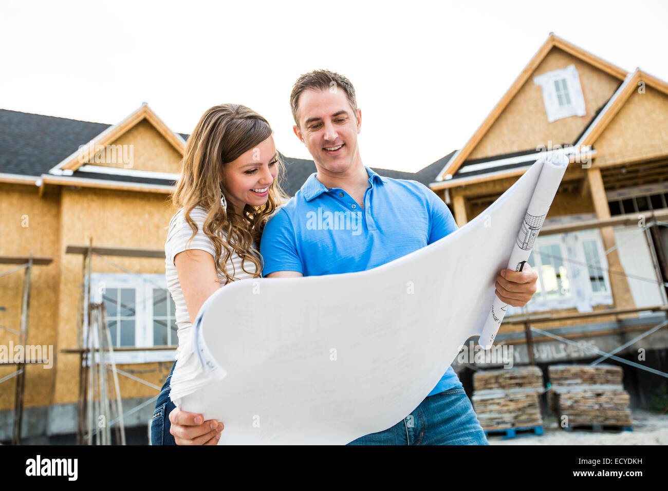 Caucasian couple reading blueprints outside house under construction ...