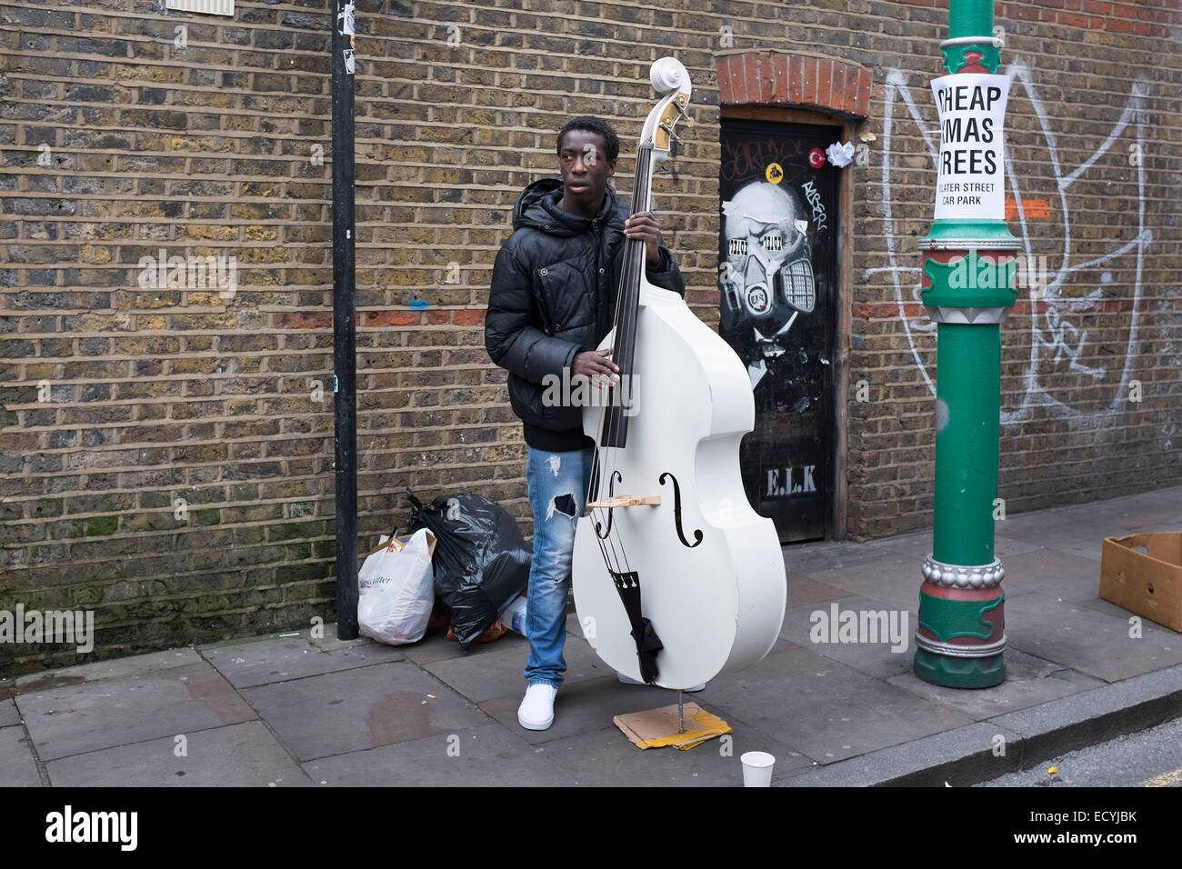 Street scene with a young busker playing a white double bass, whilst ...