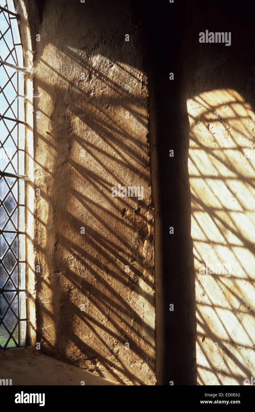 Tall diamond-leaded window casting shadows in warm sunlight onto rough ...