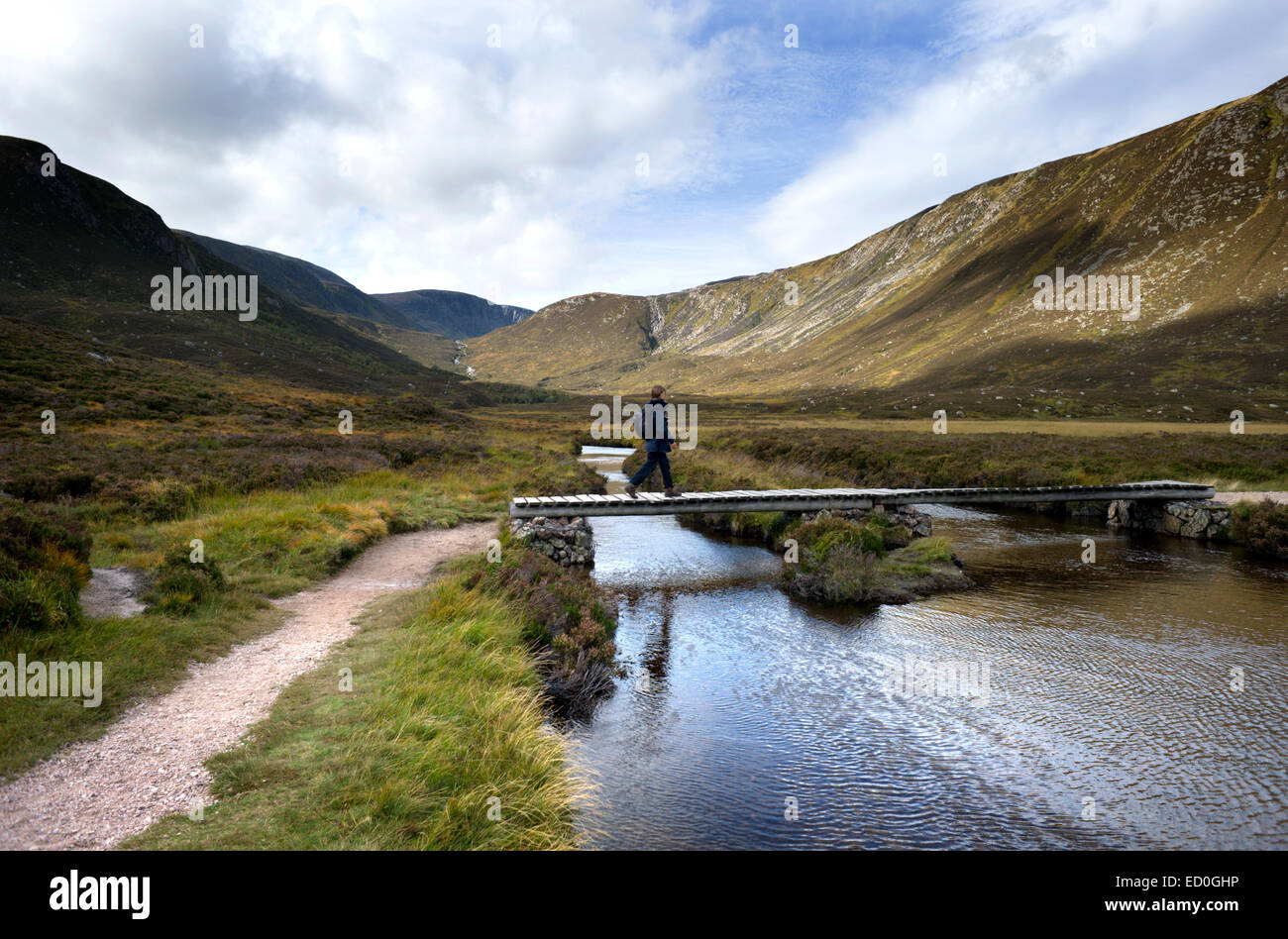 A female walker crosses a wooden footbridge over the Allt an Dubh Loch ...