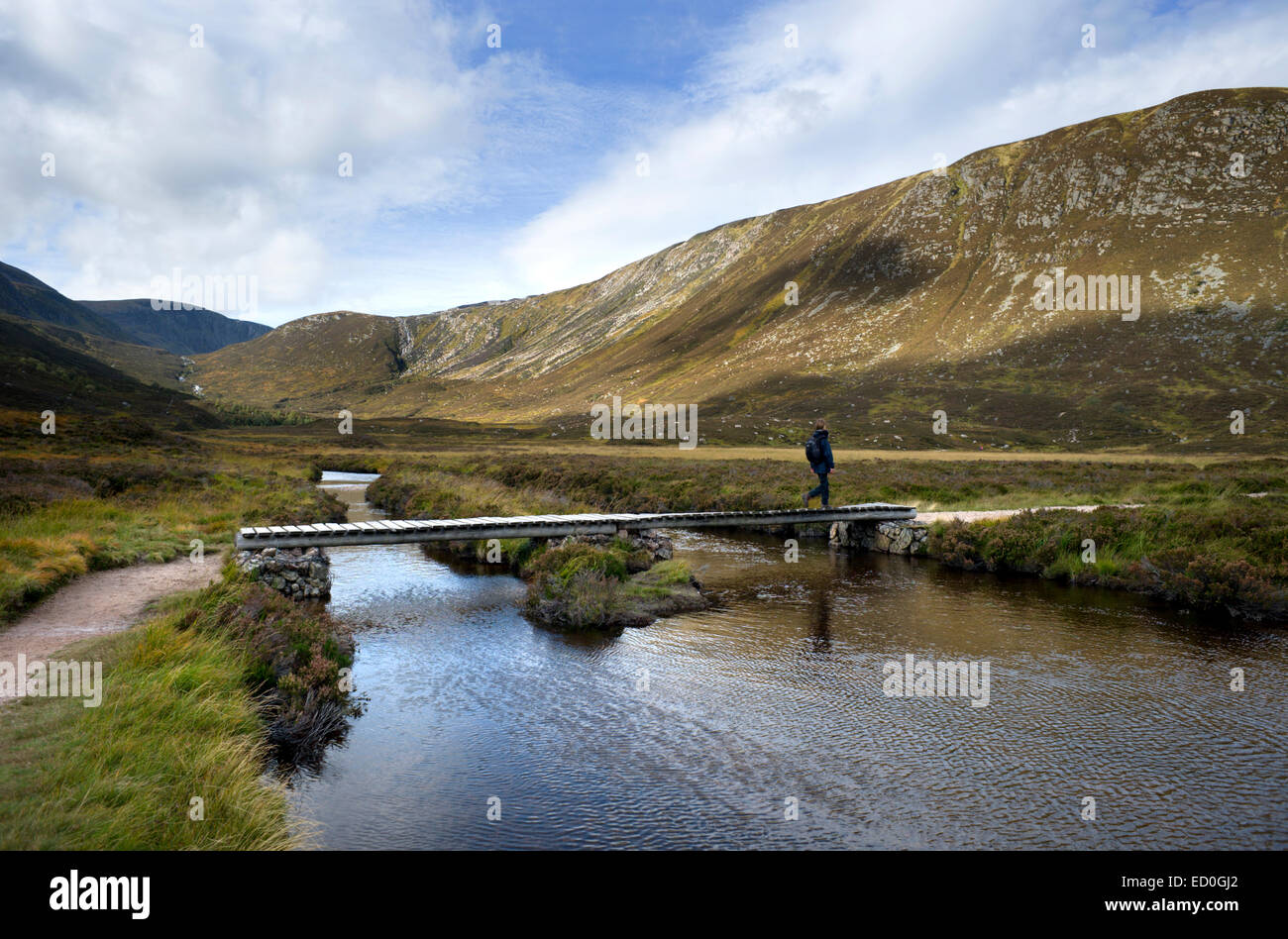A female walker crosses a wooden footbridge over the Allt an Dubh Loch ...