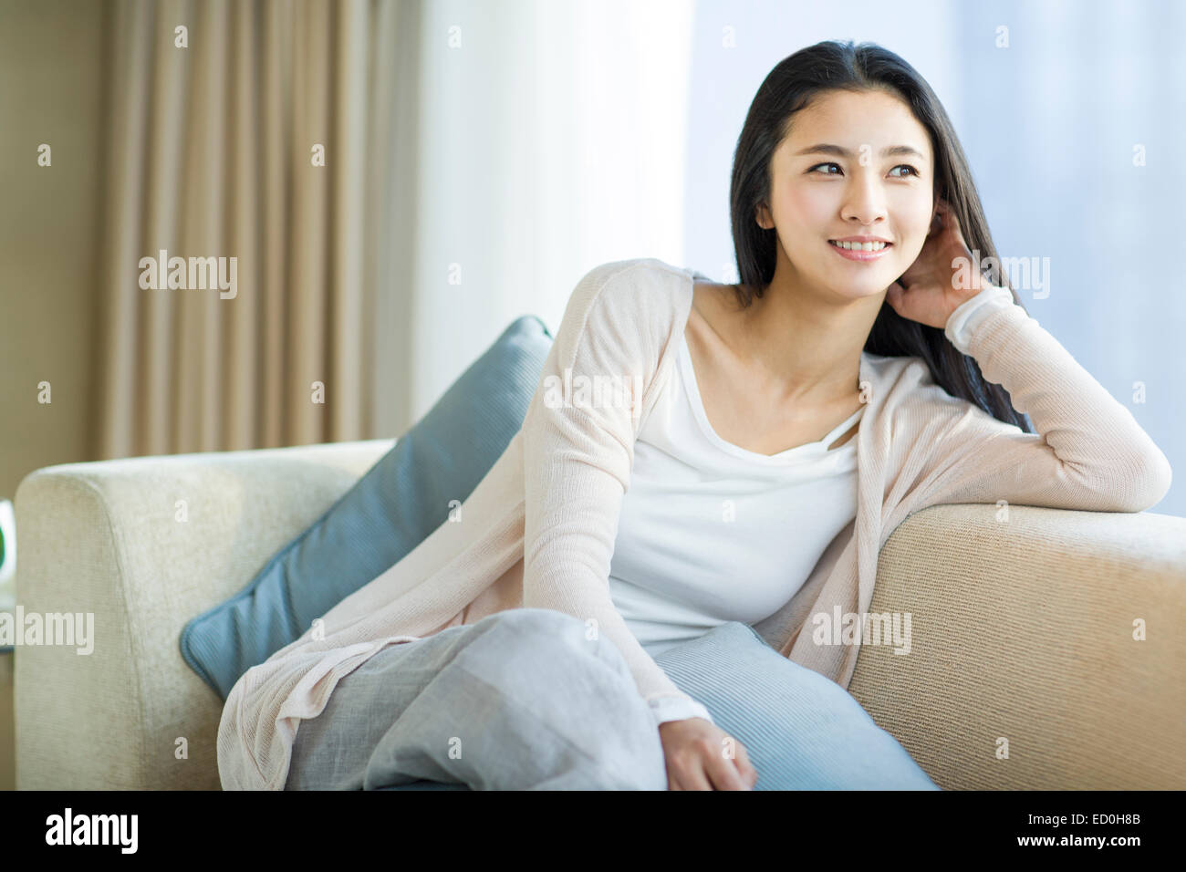 Happy young woman sitting by window Stock Photo - Alamy