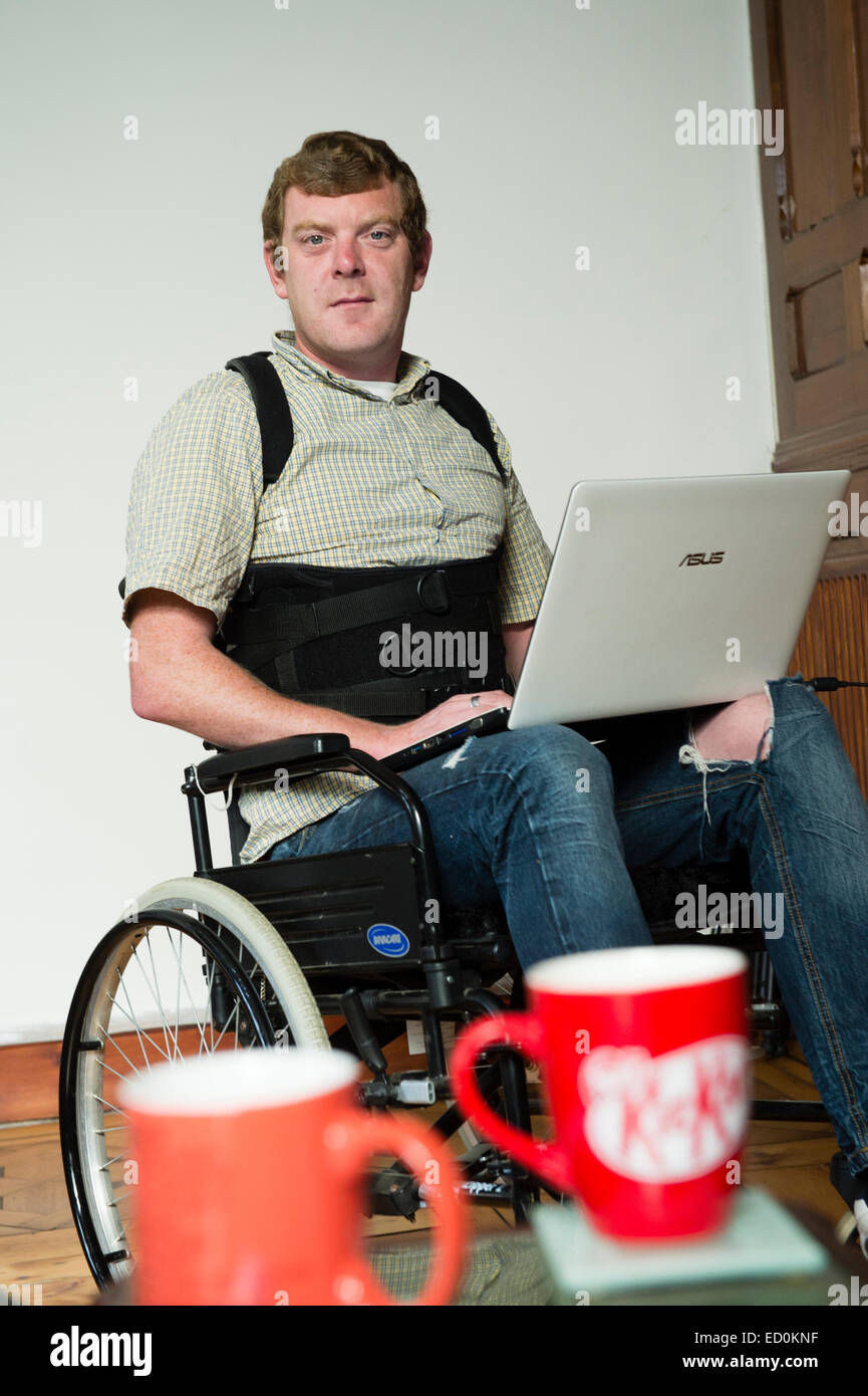 A disabled man in his wheelchair at home using his laptop computer, UK ...