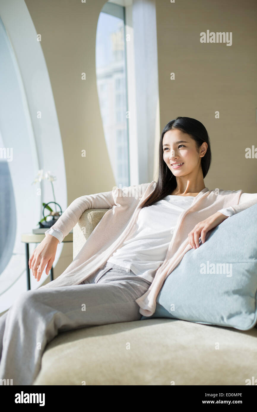 Happy young woman sitting by window Stock Photo - Alamy