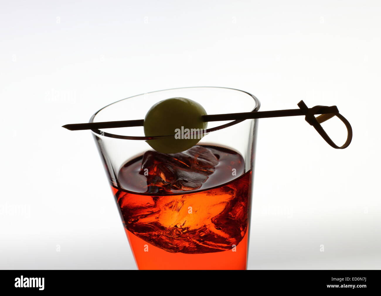 Short drink glass with red liquid, olive, ice cubes, gray background ...