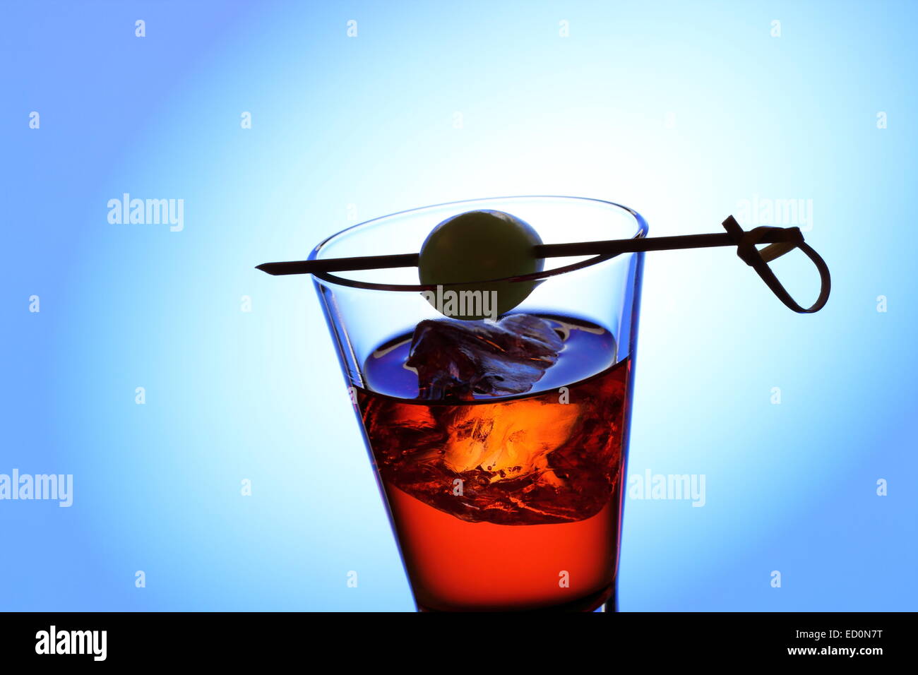 Short drink glass with red liquid, olive, ice cubes, blue background ...