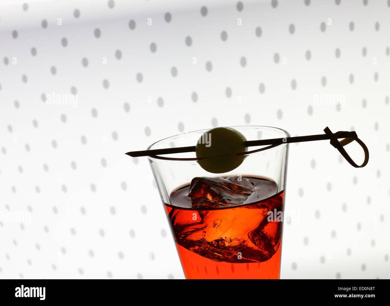 Short drink glass with red liquid, olive, ice cubes, gray dotted ...