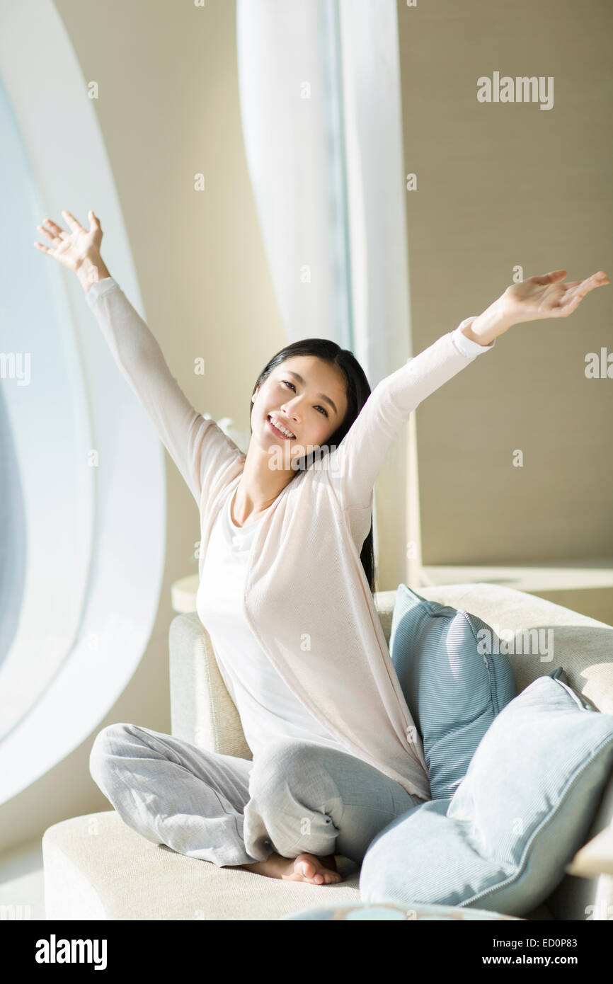 Happy young woman stretching arms on sofa Stock Photo - Alamy