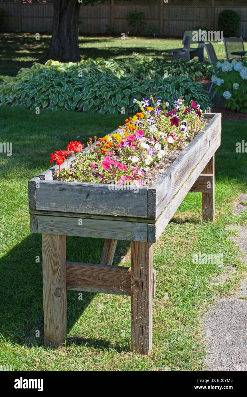 A large wood plant box with assorted flowers in a park like setting ...