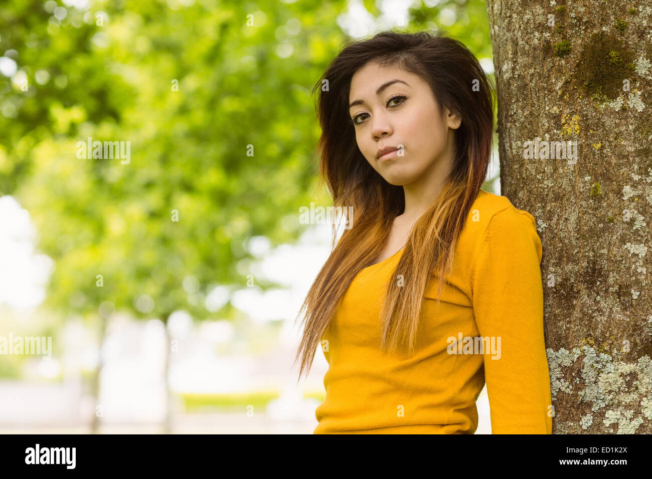 Beautiful young woman standing against tree Stock Photo - Alamy