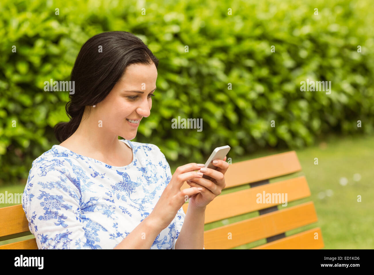 Cheerful brunette sitting on bench texting Stock Photo - Alamy