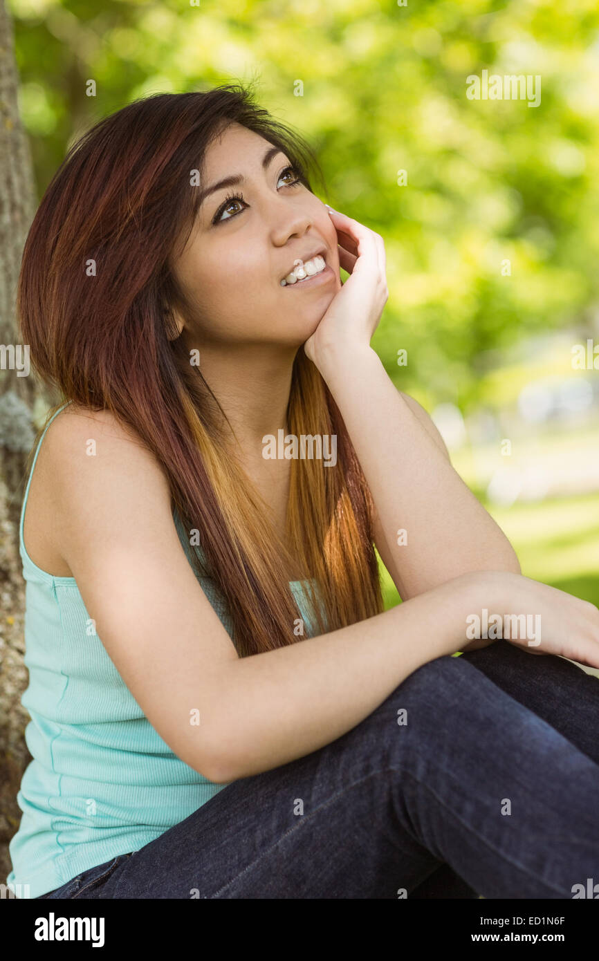 Beautiful woman sitting against tree in park Stock Photo - Alamy