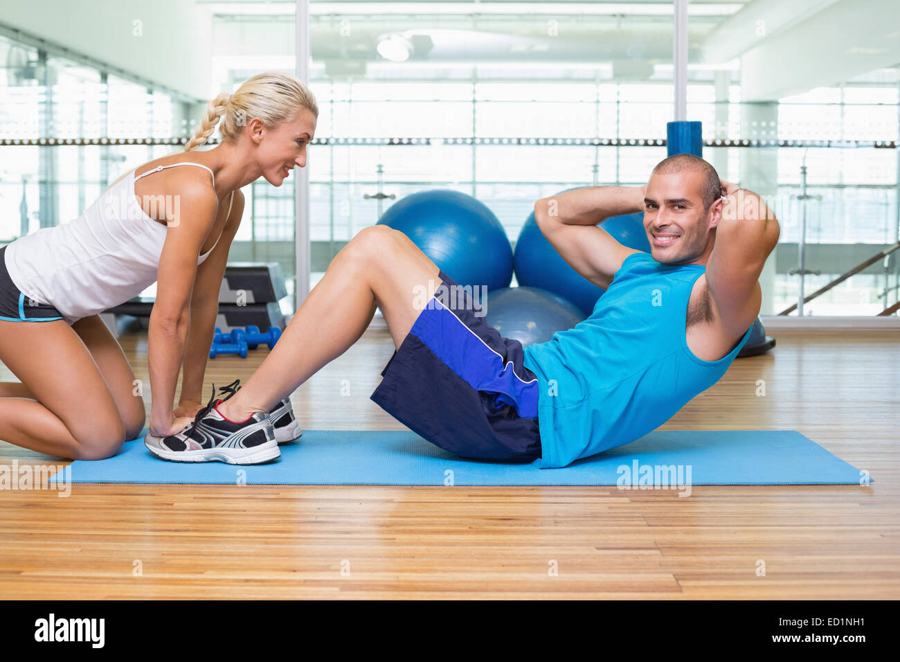 Trainer assisting young man with abdominal crunches at fitness studio ...
