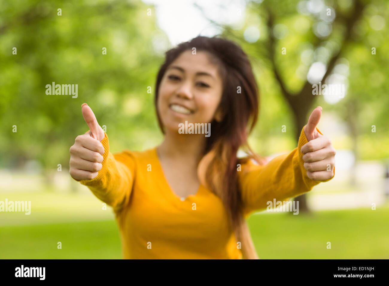 Beautiful woman gesturing thumbs up in park Stock Photo - Alamy