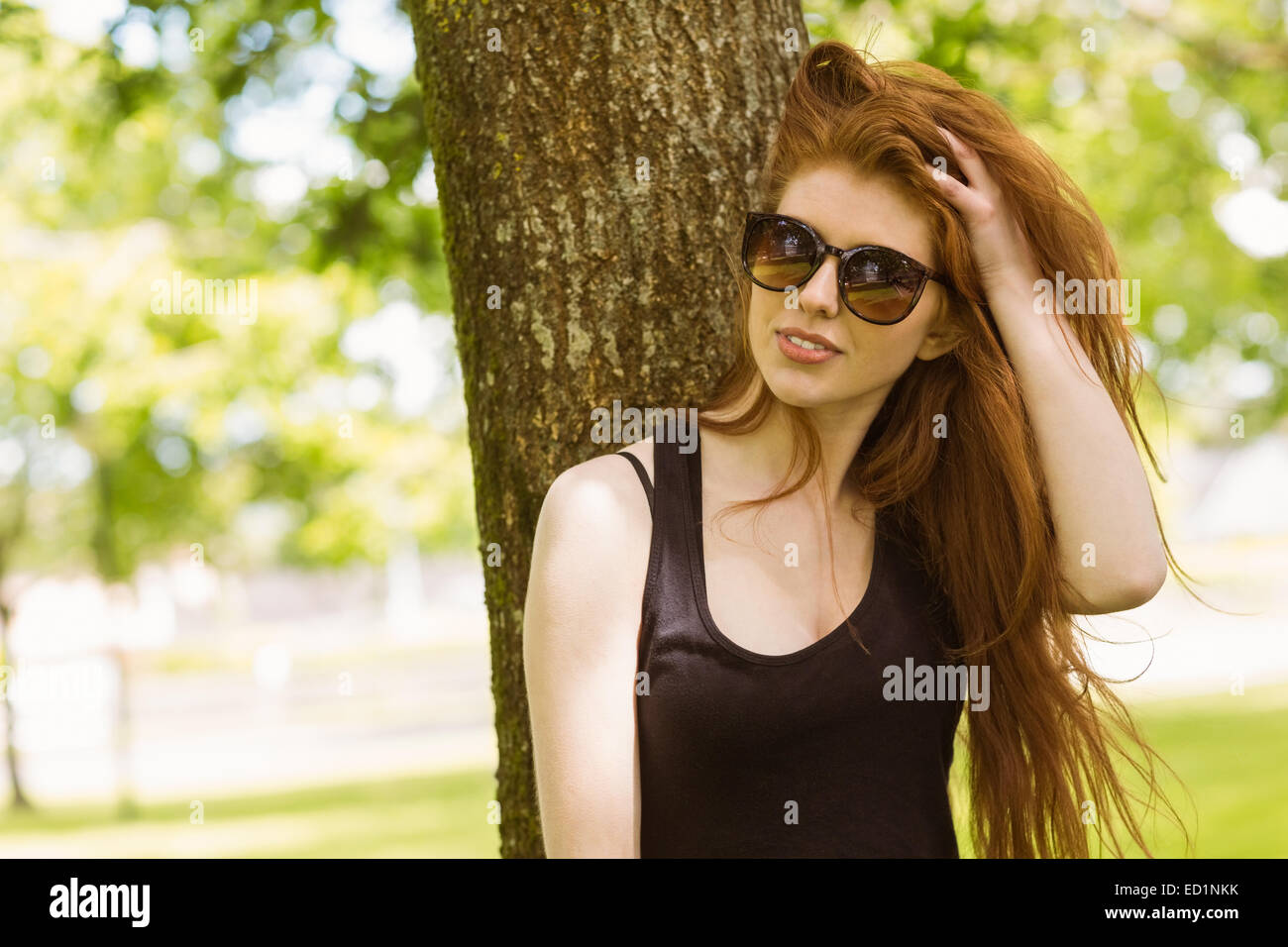 Beautiful young woman against tree in park Stock Photo - Alamy