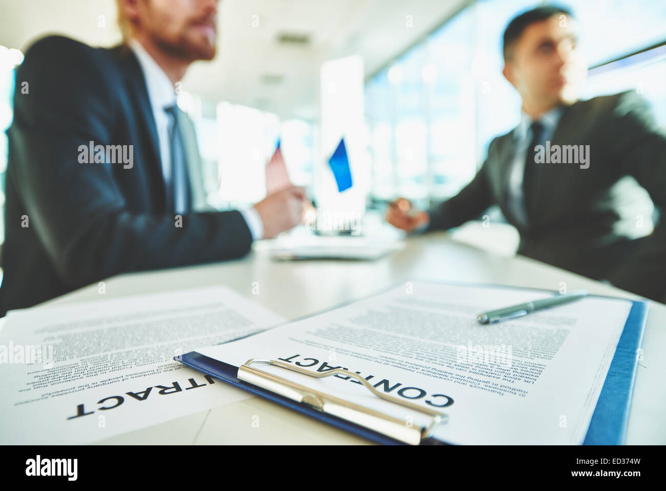 Business contracts on the desk with two male colleagues sitting on ...