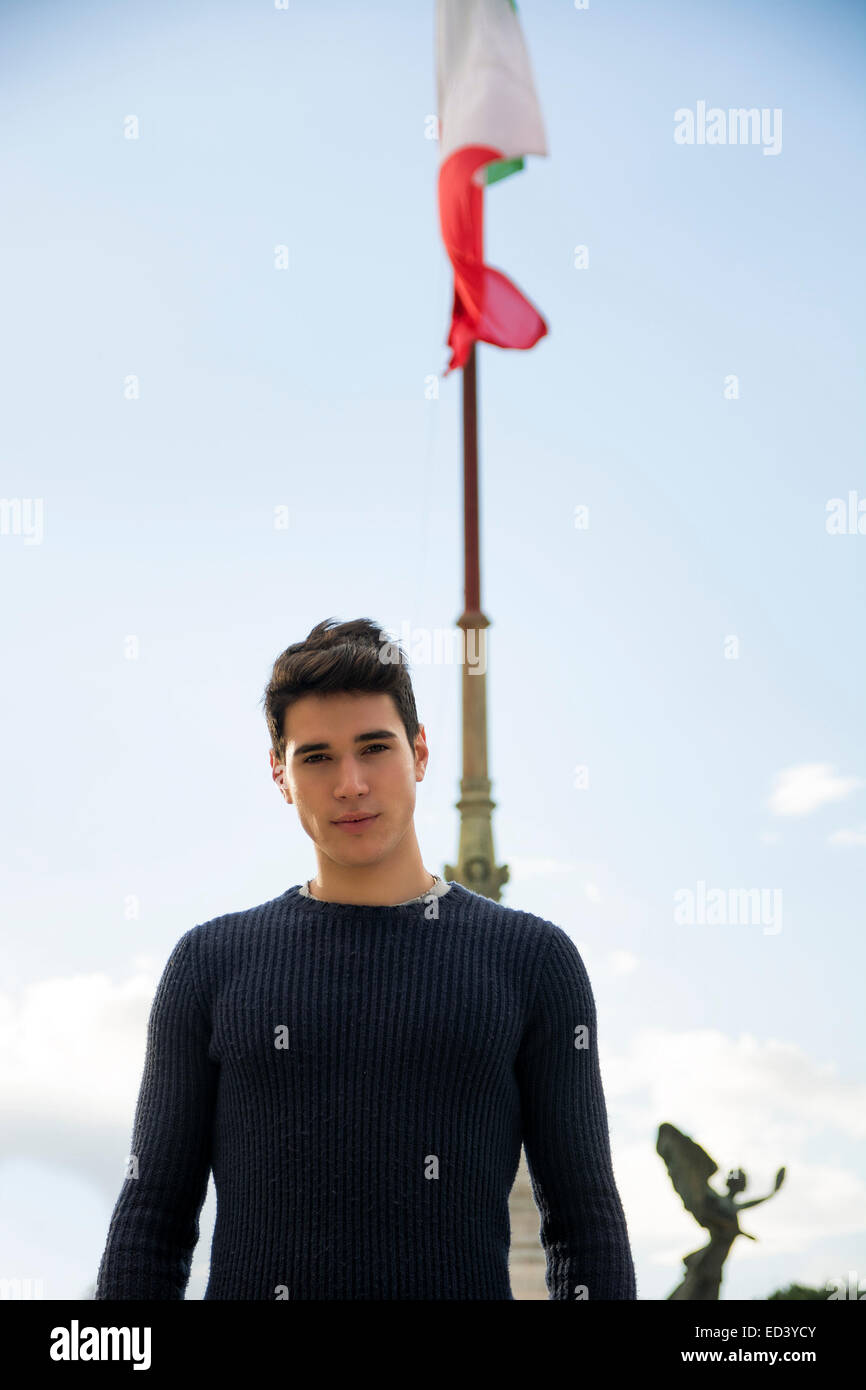 Handsome young man in front of Italian flag against blue sky in Rome ...