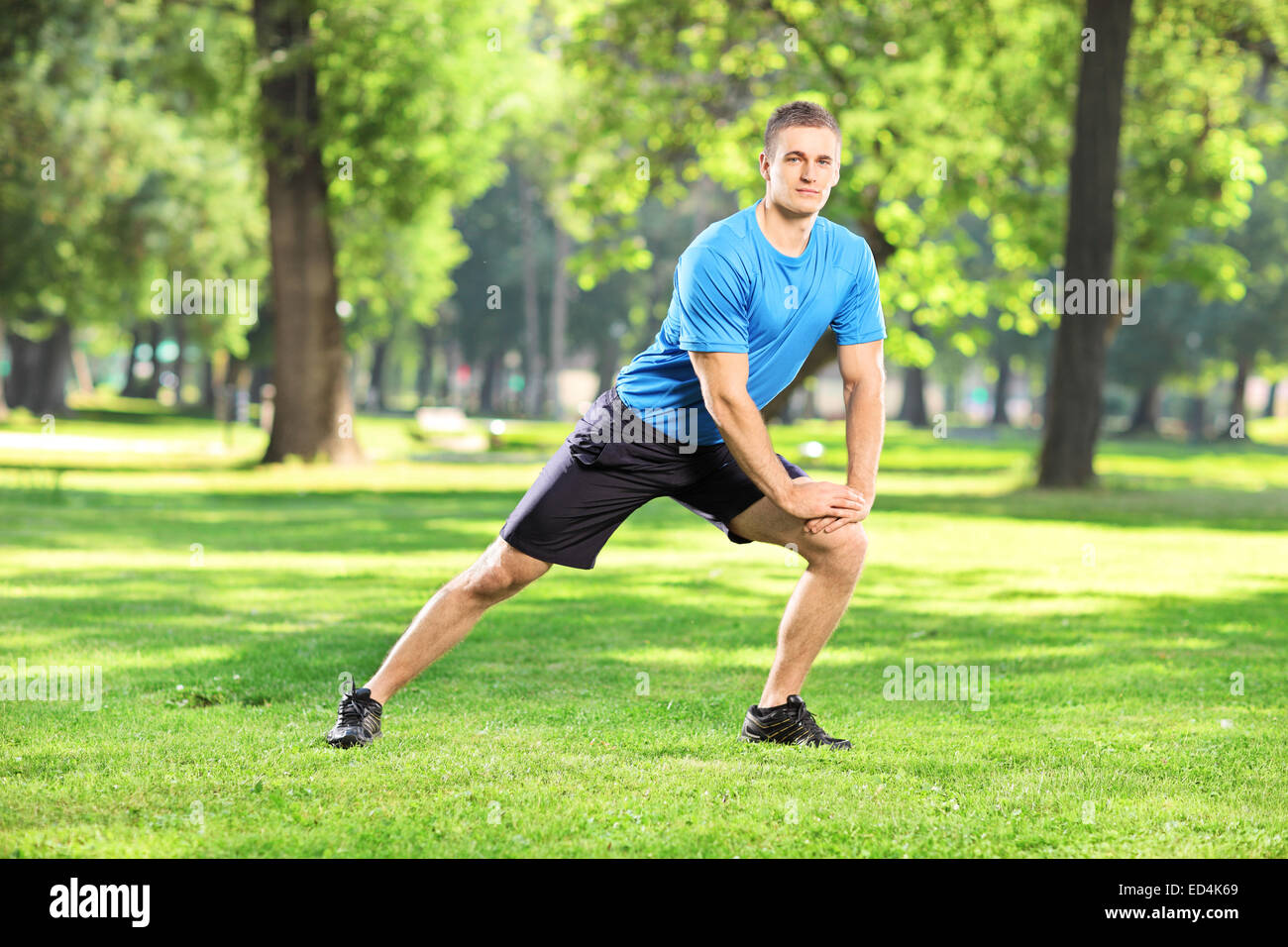 Full length portrait of a young smiling athlete exercising in a park ...