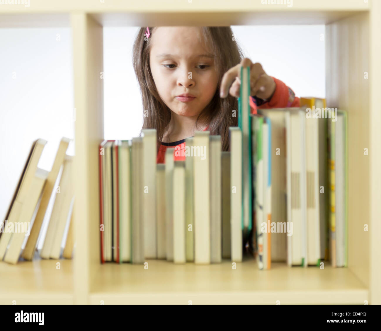 Young girl taking book from bookshelf, behind shelf. Horizontal Stock ...