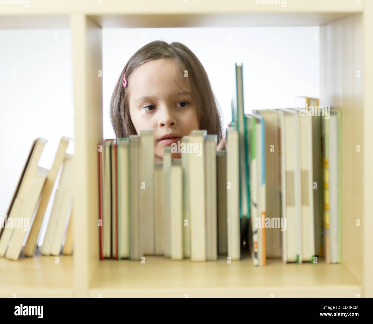 Young girl looking through books in library behind shelf. Horizontal ...