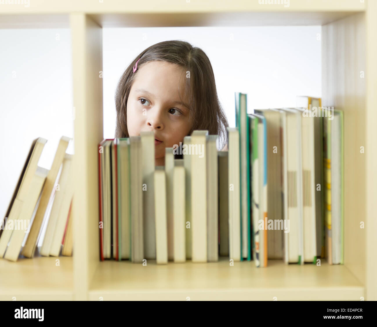 Young girl looking through books in library behind shelf. Horizontal ...