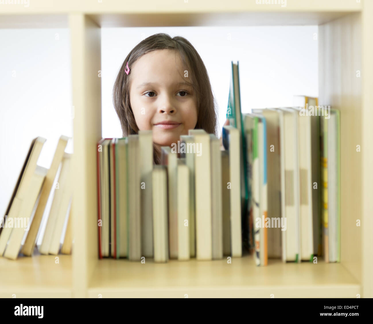 Young girl looking through books in library behind shelf. Horizontal ...