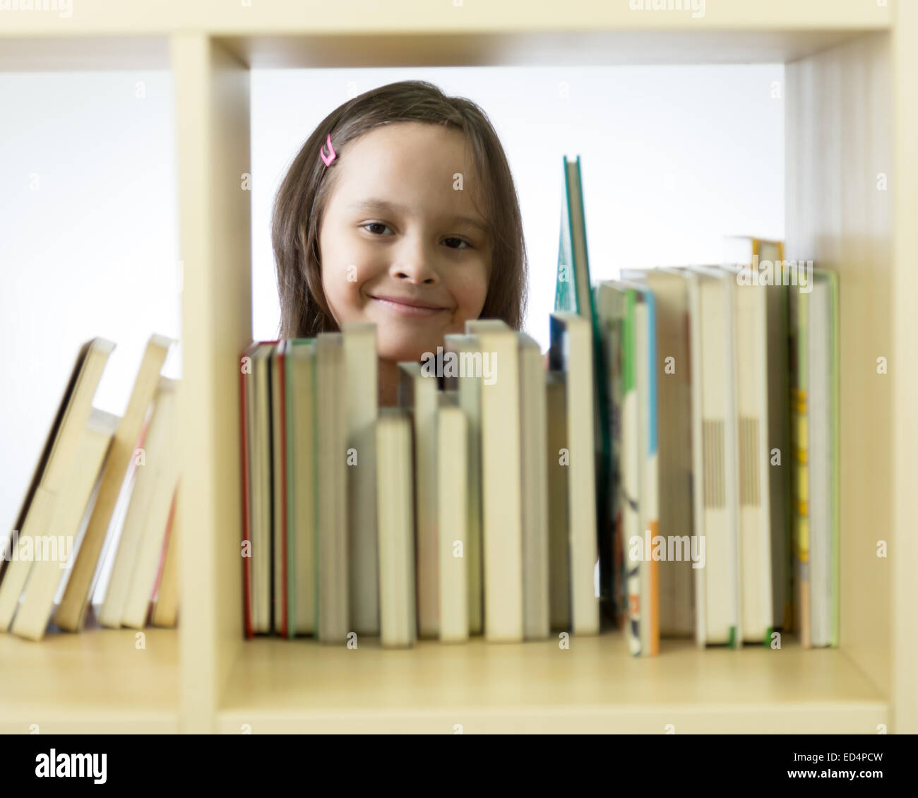 Young girl looking through books in library behind shelf. Horizontal ...