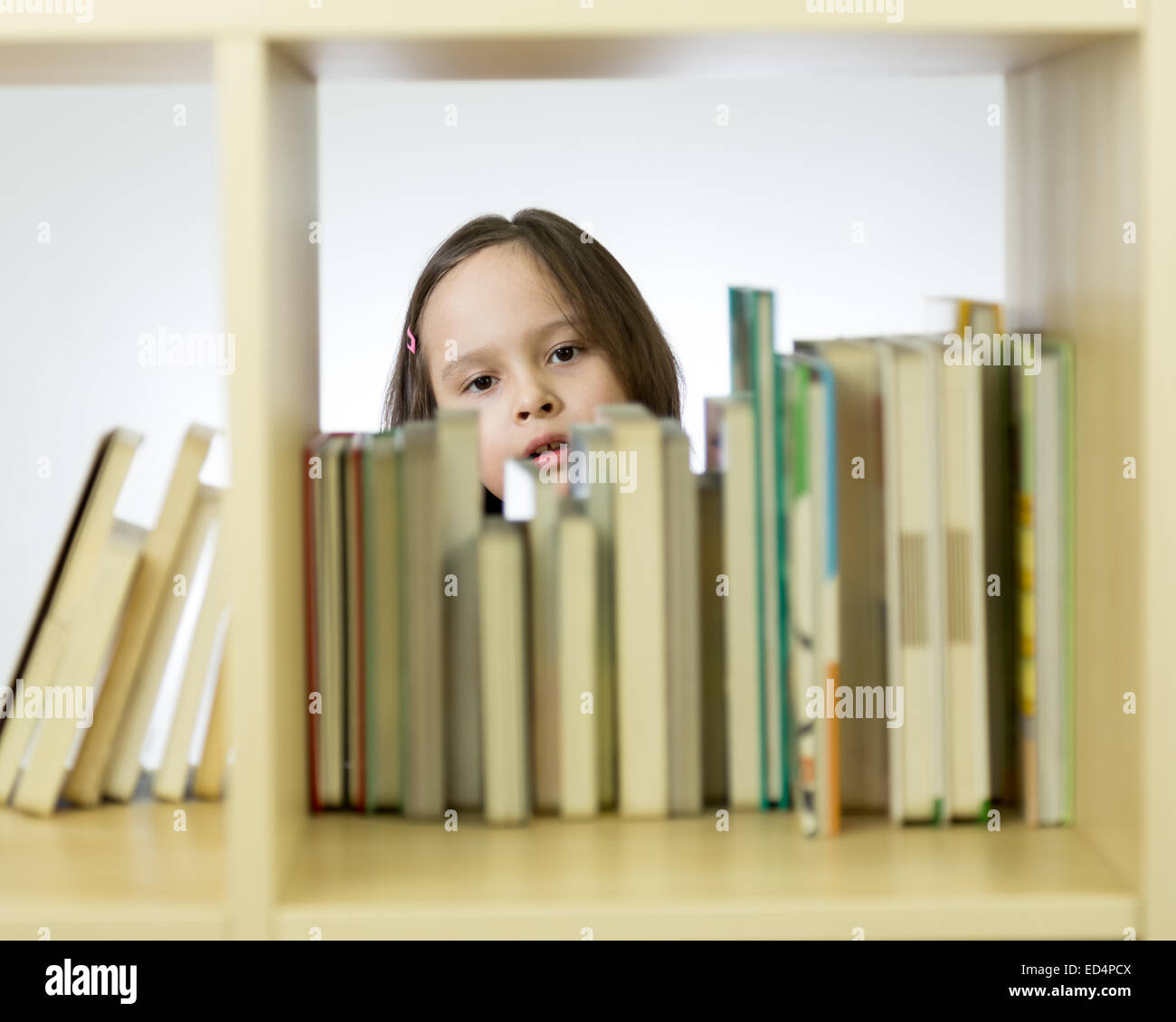 Young girl looking through books in library behind shelf. Horizontal ...