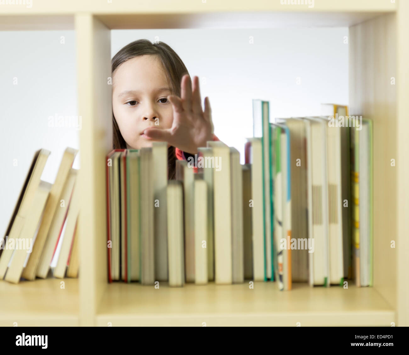 Young girl looking through books in library behind shelf. Horizontal ...