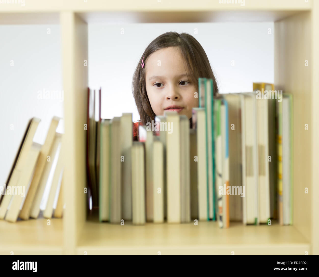 Young girl looking through books in library behind shelf. Horizontal ...