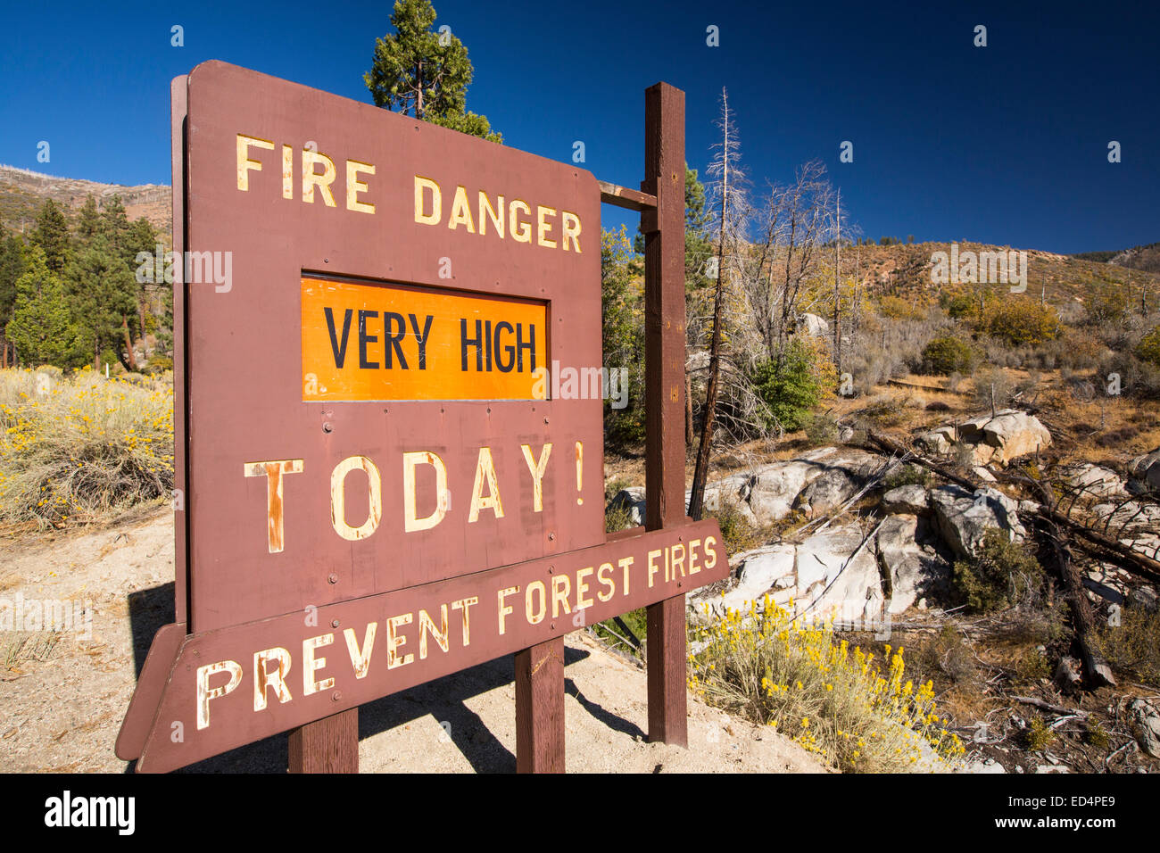 A fire danger sign next to forest that has been burnt by a fire in the ...