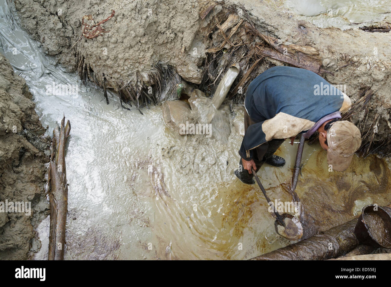 A worker collects oil remnants of traditional mining waste disposal in ...
