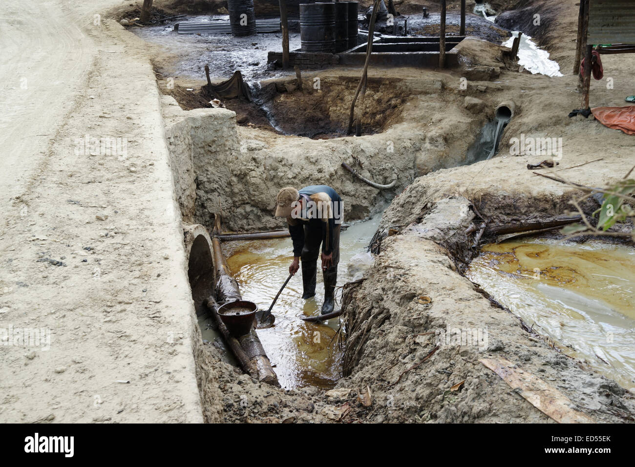 A worker collects oil remnants of traditional mining waste disposal in ...