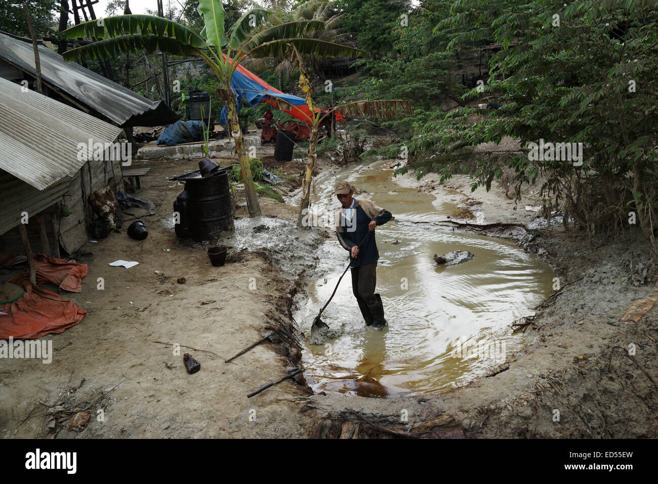 A worker collects oil remnants of traditional mining waste disposal in ...