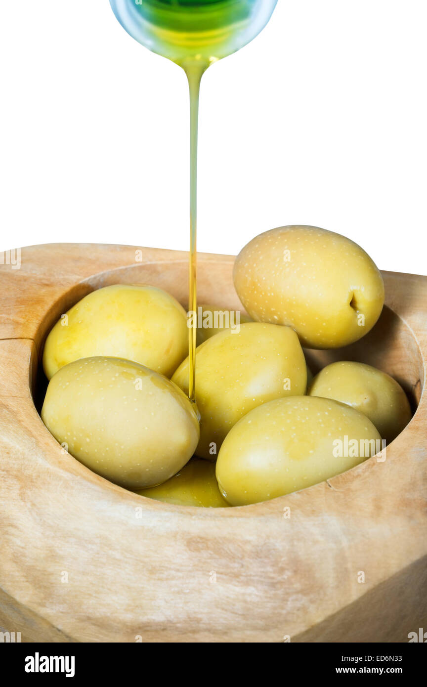 olive oil in thin trickle flows from bottle on green olives in wooden ...