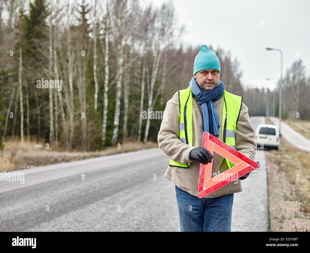 Mid adult man wearing reflector vest and he have a red warning triangle ...