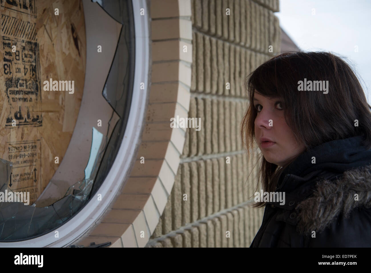 A young woman looks around as she discovers a broken window Stock Photo ...